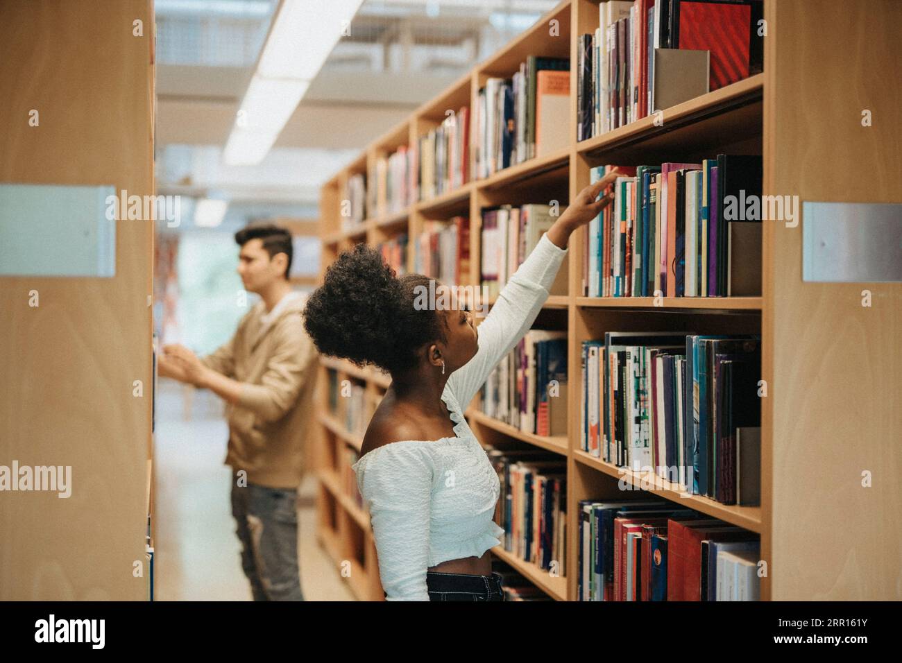 Side view of student searching books on bookshelf in library at ...
