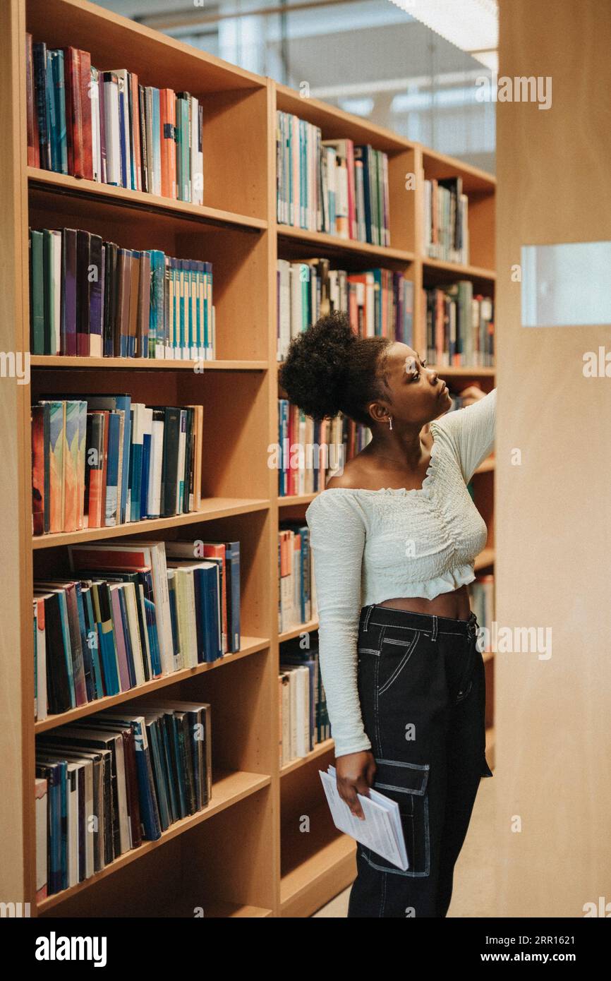 Female student searching books on shelf in library at university Stock ...