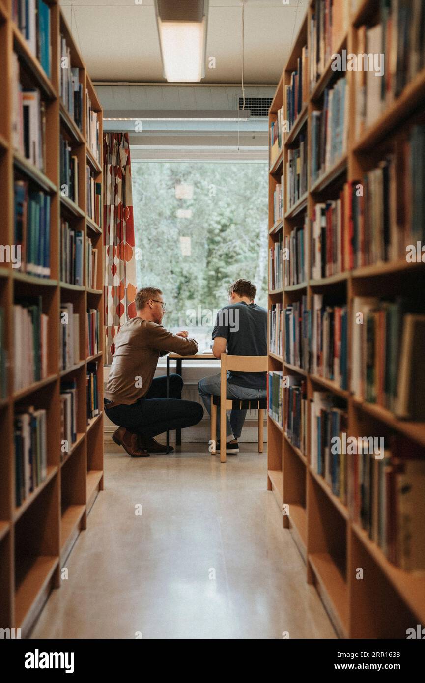 Professor explaining student studying in library at university Stock ...