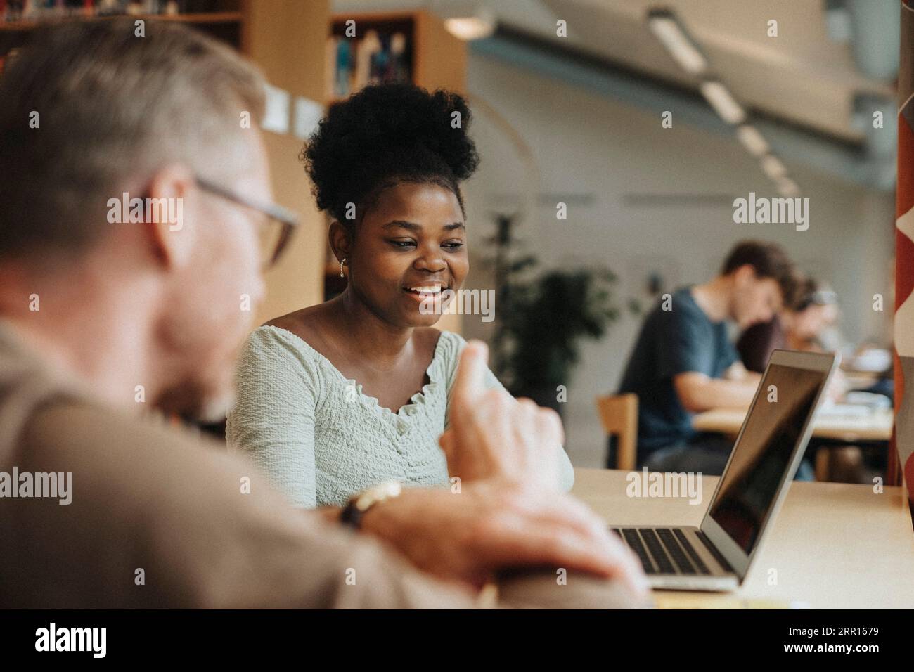 Smiling student discussing with professor over laptop in library at ...