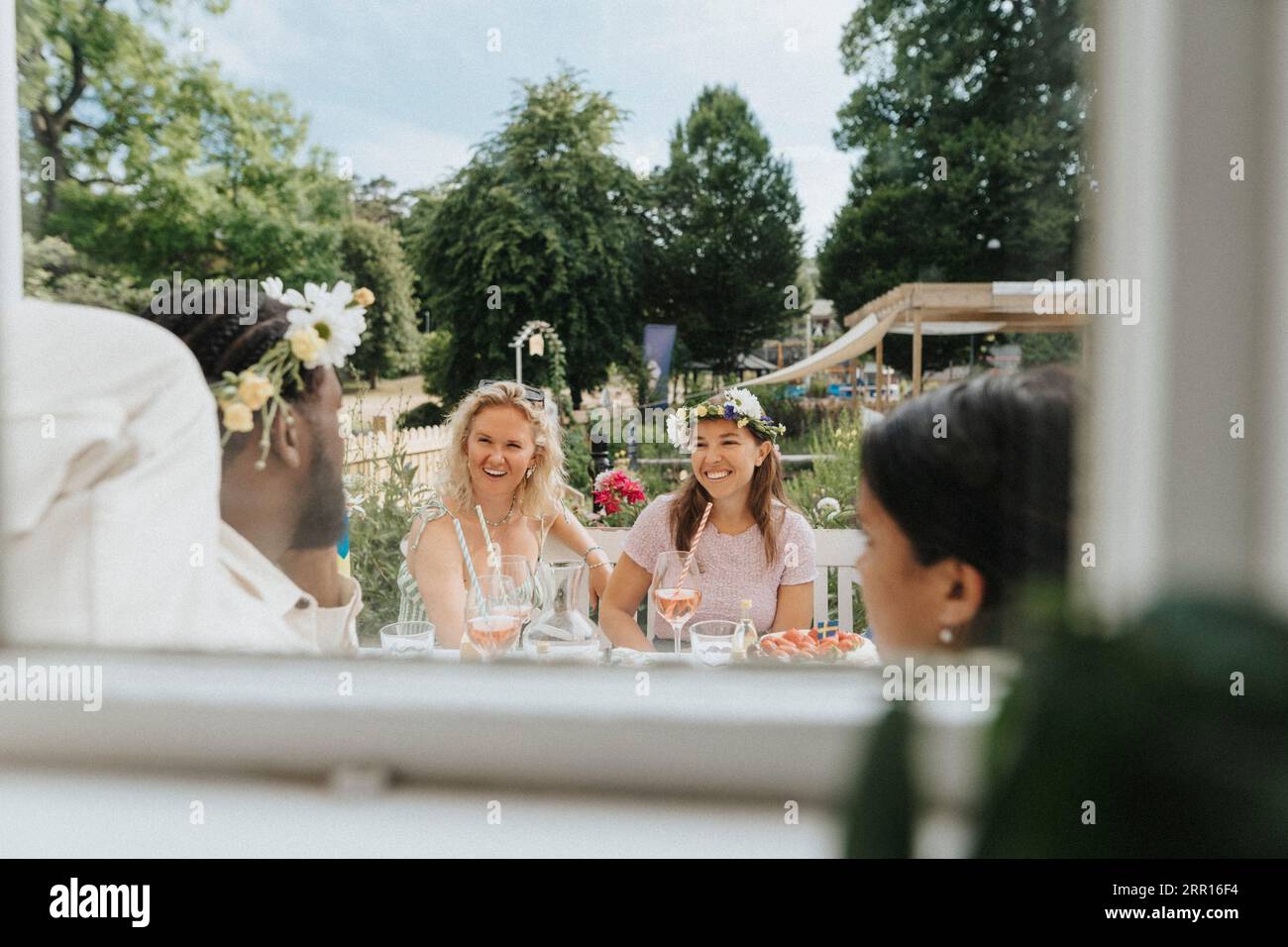 Happy young women enjoying with friends at dinner party seen through ...