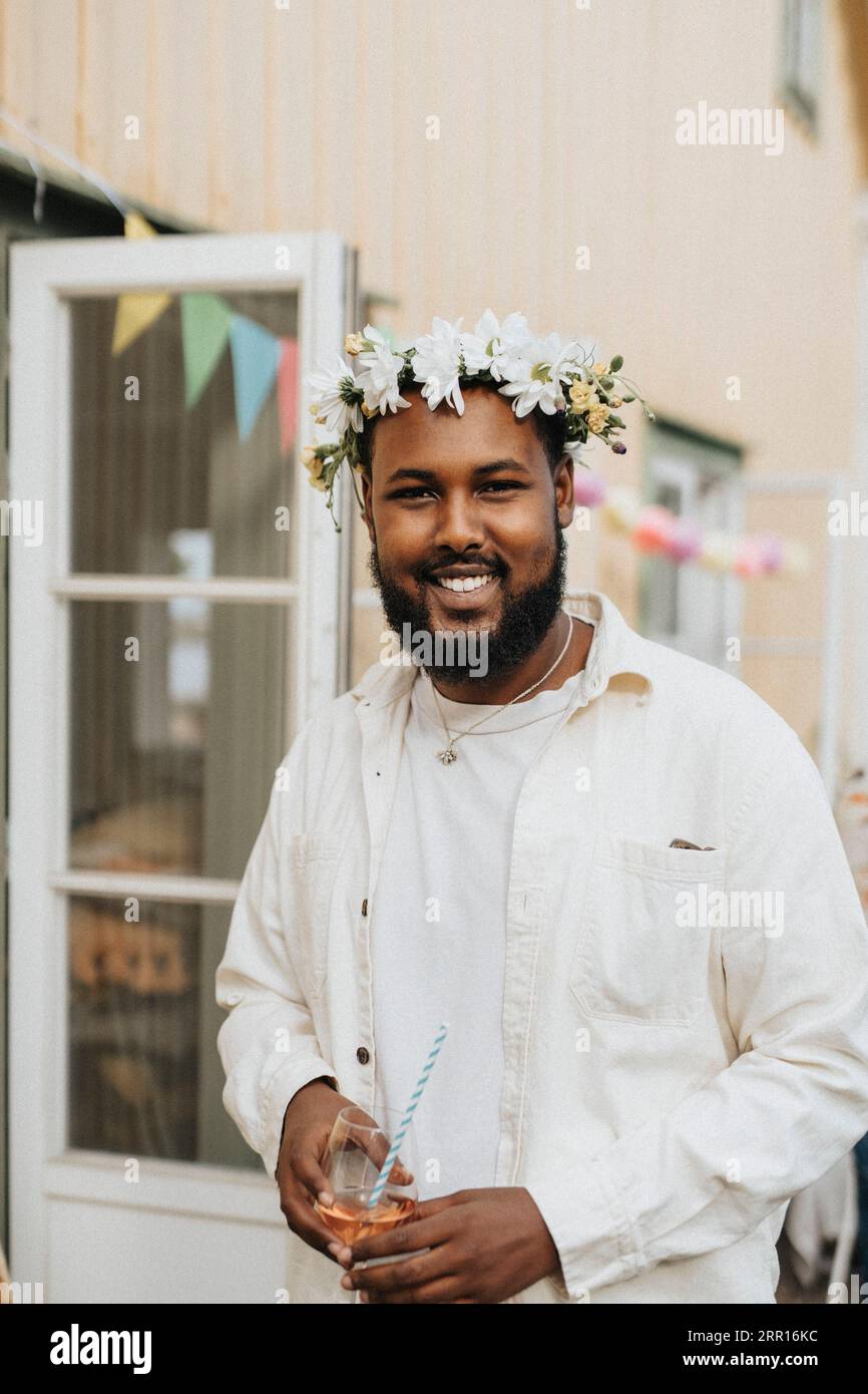 Portrait of smiling young man wearing tiara while holding wineglass ...