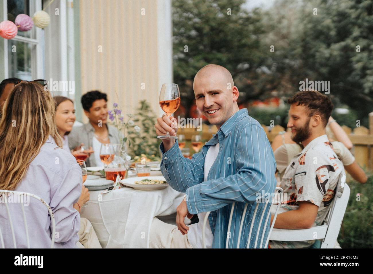Side view portrait of smiling young man holding wineglass while sitting ...