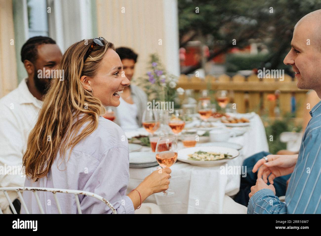 Happy young woman holding wineglass while laughing with male friend ...