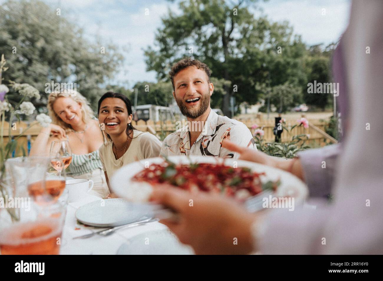 Happy male and female friends laughing while sitting at table during ...