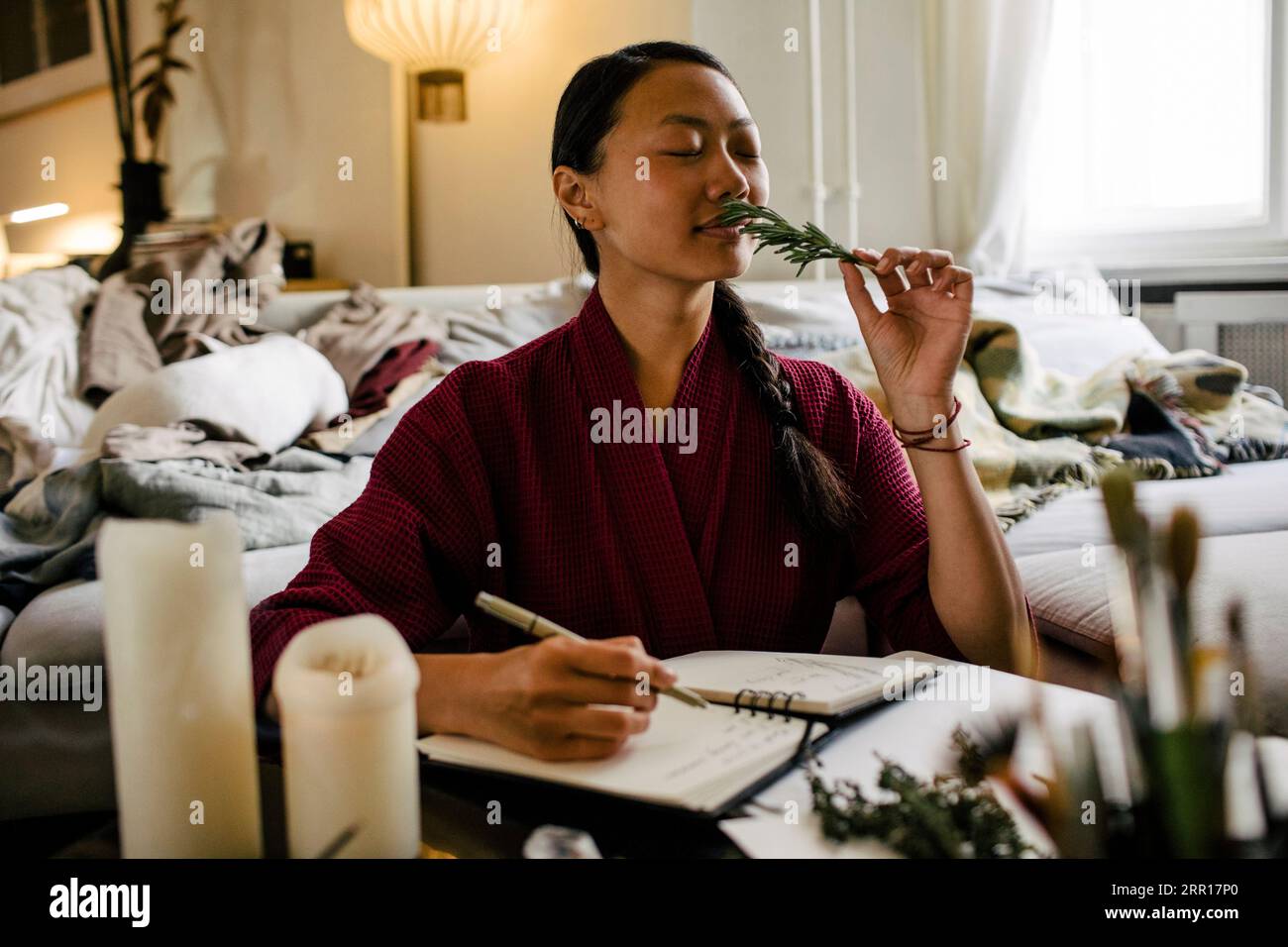 Young woman smelling herbs while while writing in book at home Stock ...