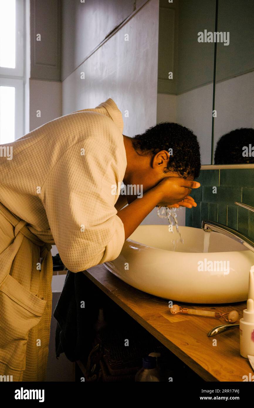 Side view of young woman washing face at sink in bathroom Stock Photo ...