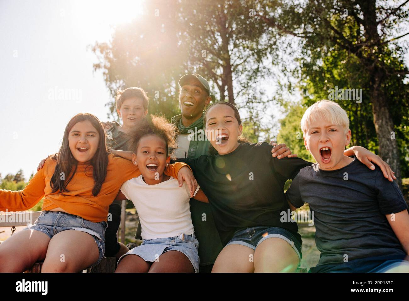 Cheerful camp counselor sitting with kids screaming at summer camp ...