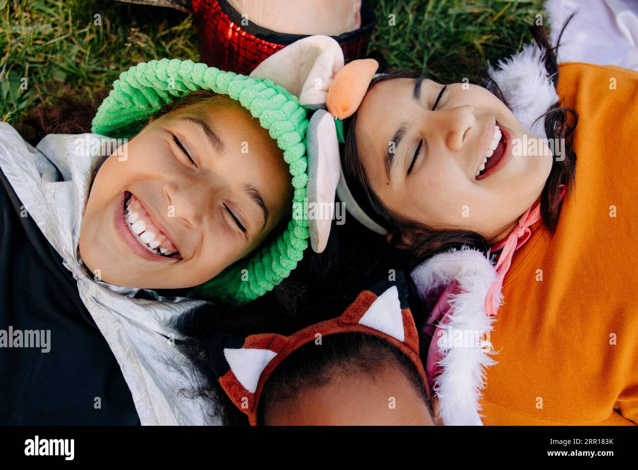 Carefree kids with eyes closed laughing while lying on grass at summer ...