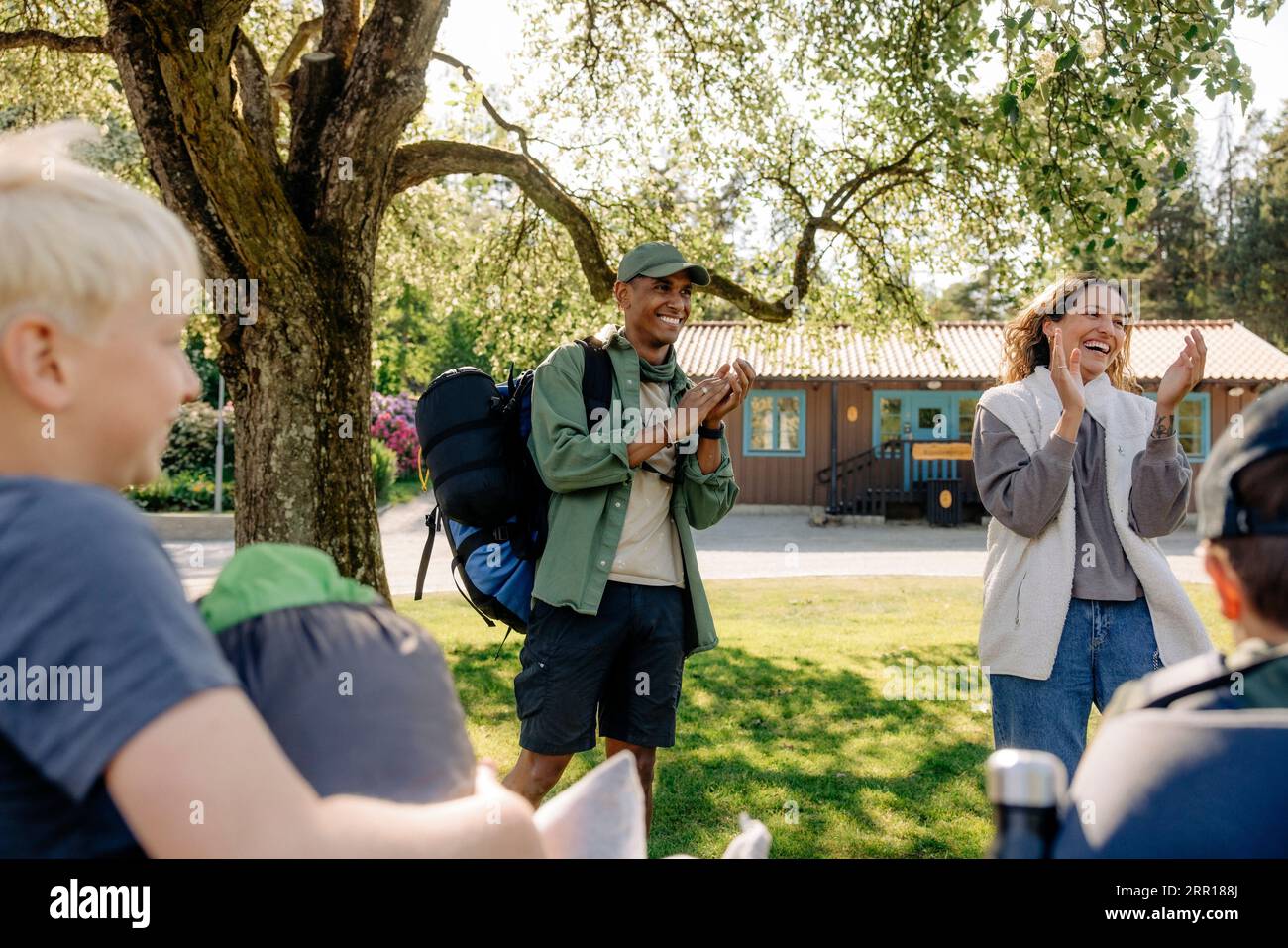Happy male and female camp counselor clapping while standing with kids ...