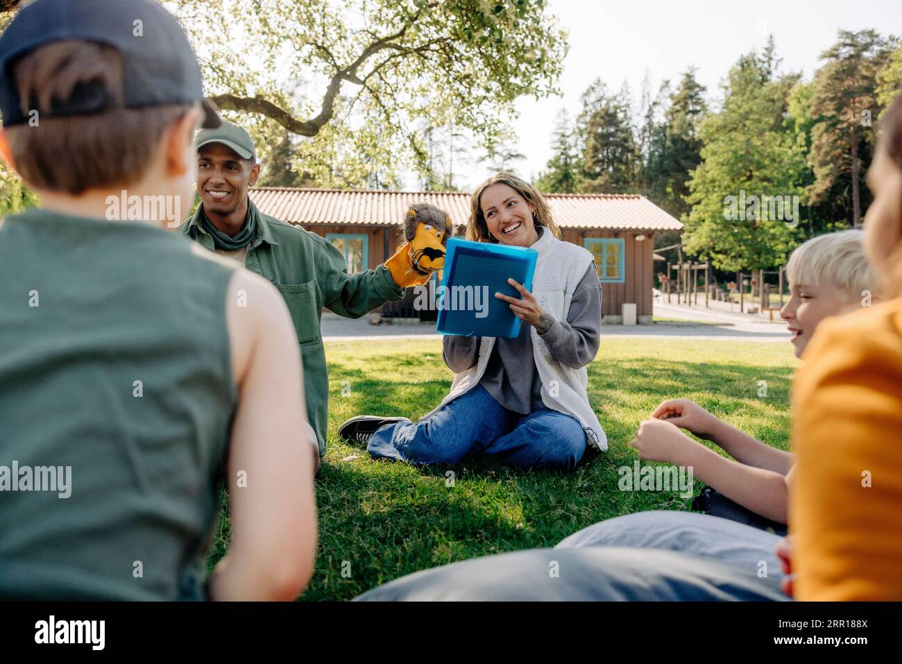 Camp counselors playing with kids while sitting on grass at summer camp ...