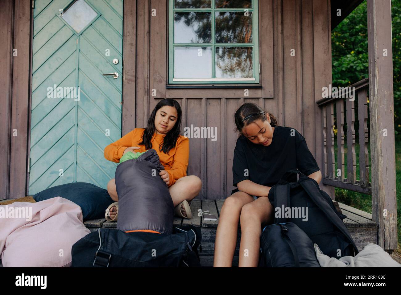 Girls unpacking backpacks while sitting on porch outside cabin Stock ...
