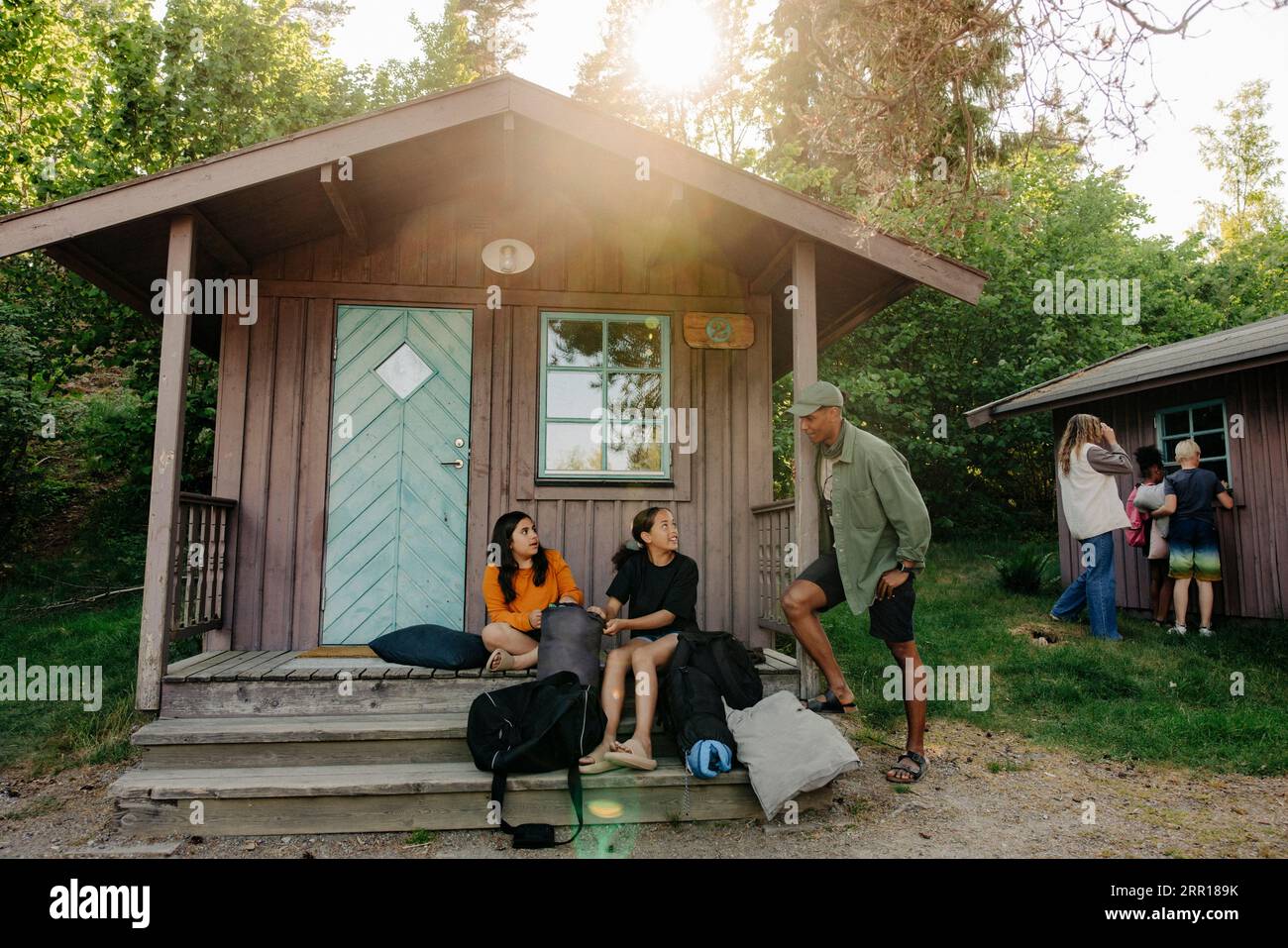 Male counselor talking to girls sitting on porch outside cabin at ...