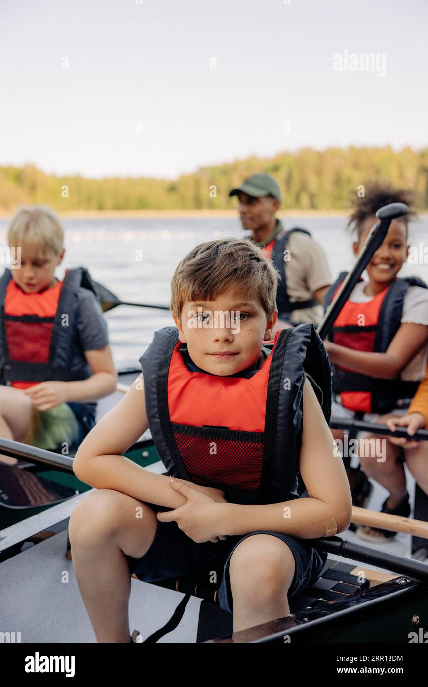 Portrait of boy wearing life jacket while sitting in kayak at summer ...
