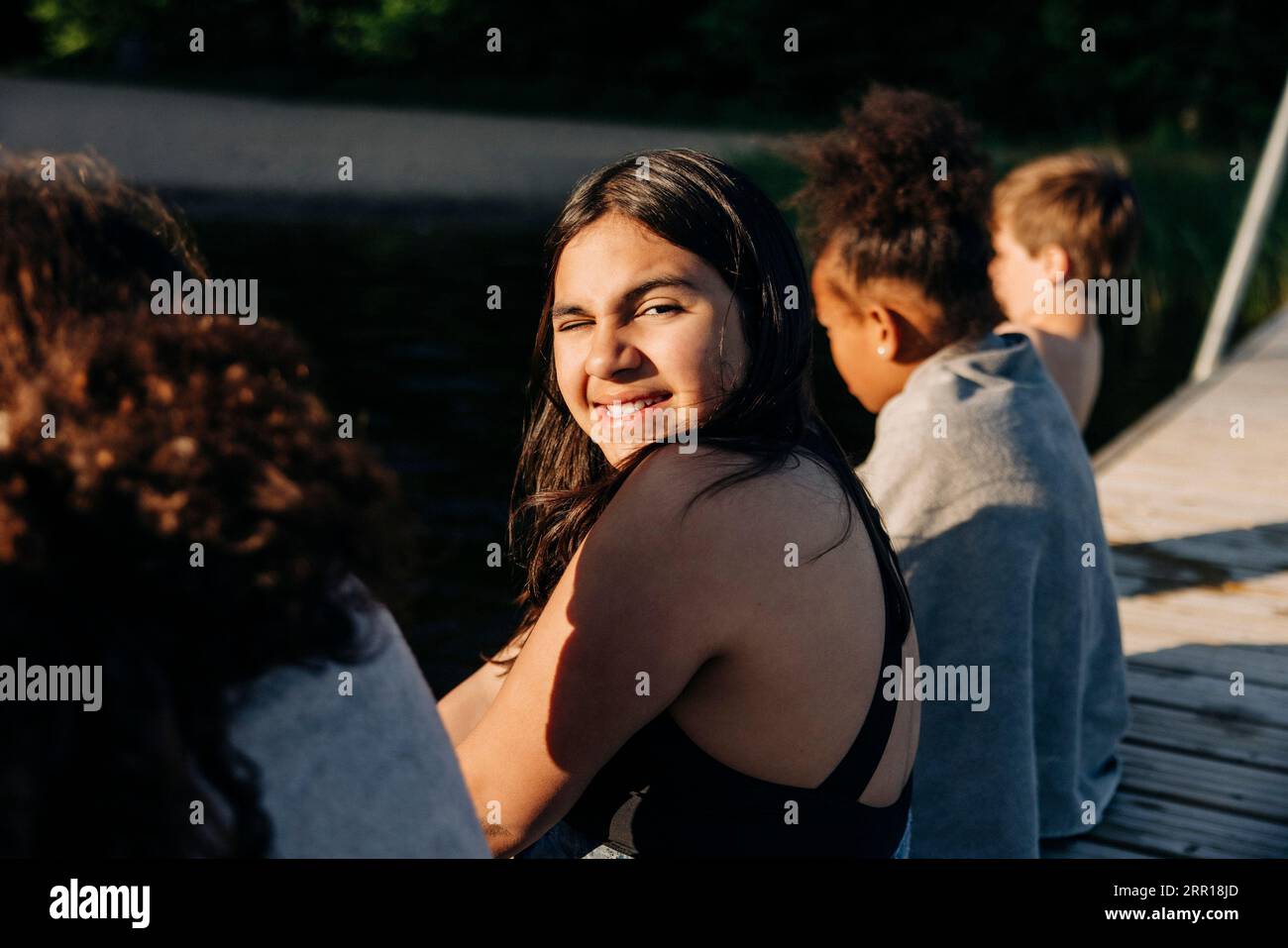 Side view portrait of smiling girl winking while sitting with friends ...