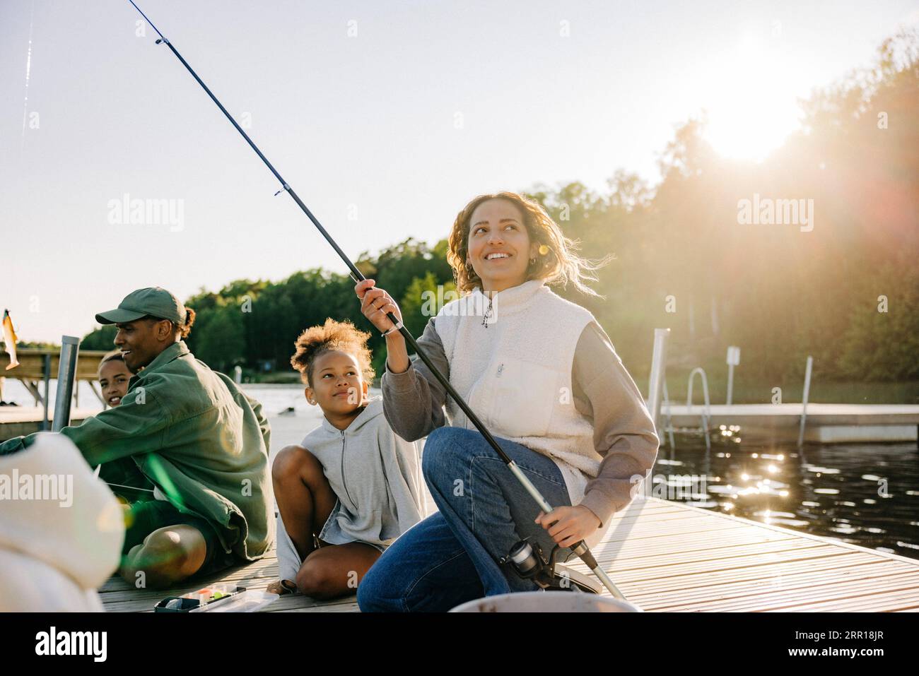 Female counselor holding fishing rod while sitting next to girl on ...