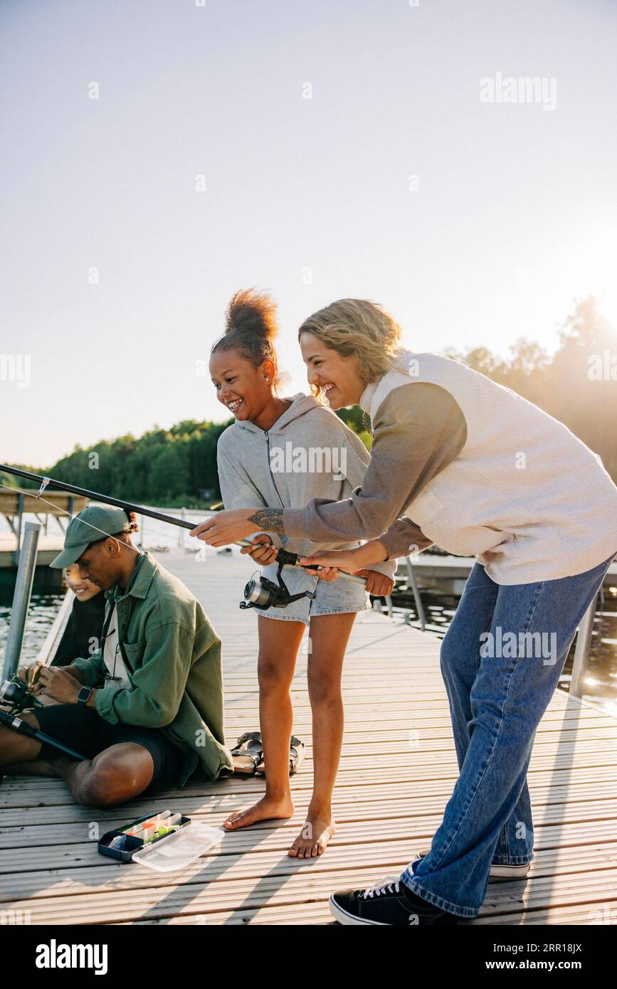 Happy counselor doing fishing with girl standing on jetty by lake at ...