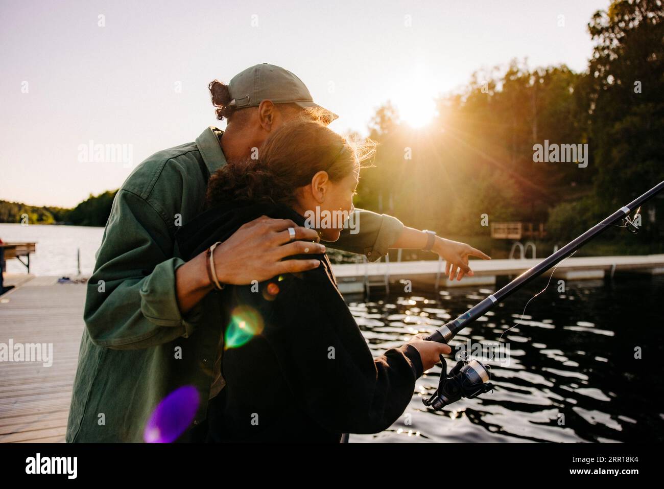 Male counselor gesturing by girl fishing on jetty near lake at summer ...