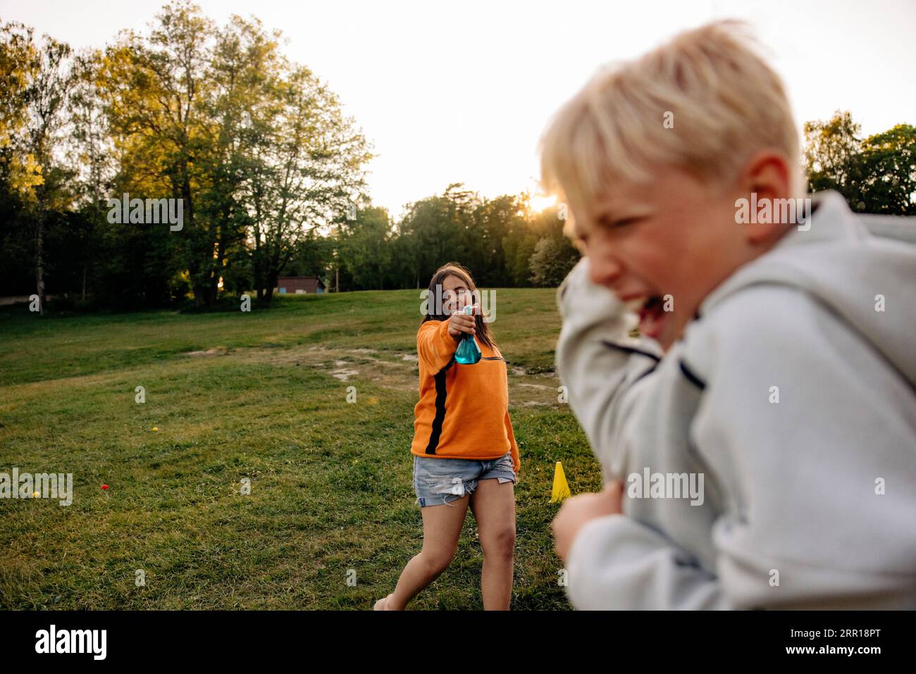 Girl spraying water on male friend while playing in playground at ...