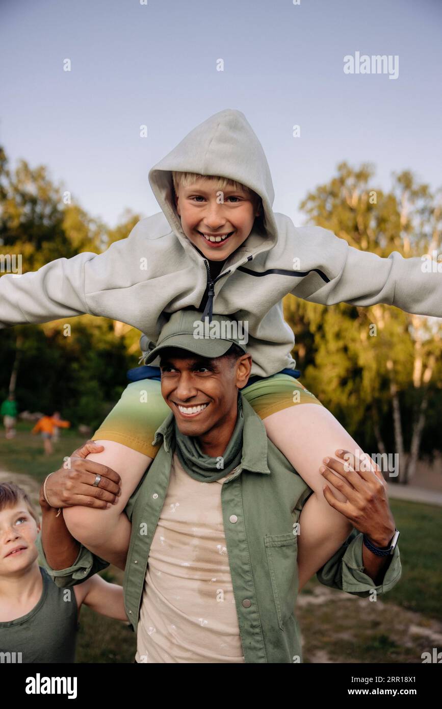 Male camp counselor carrying boy on shoulders while having fun in ...