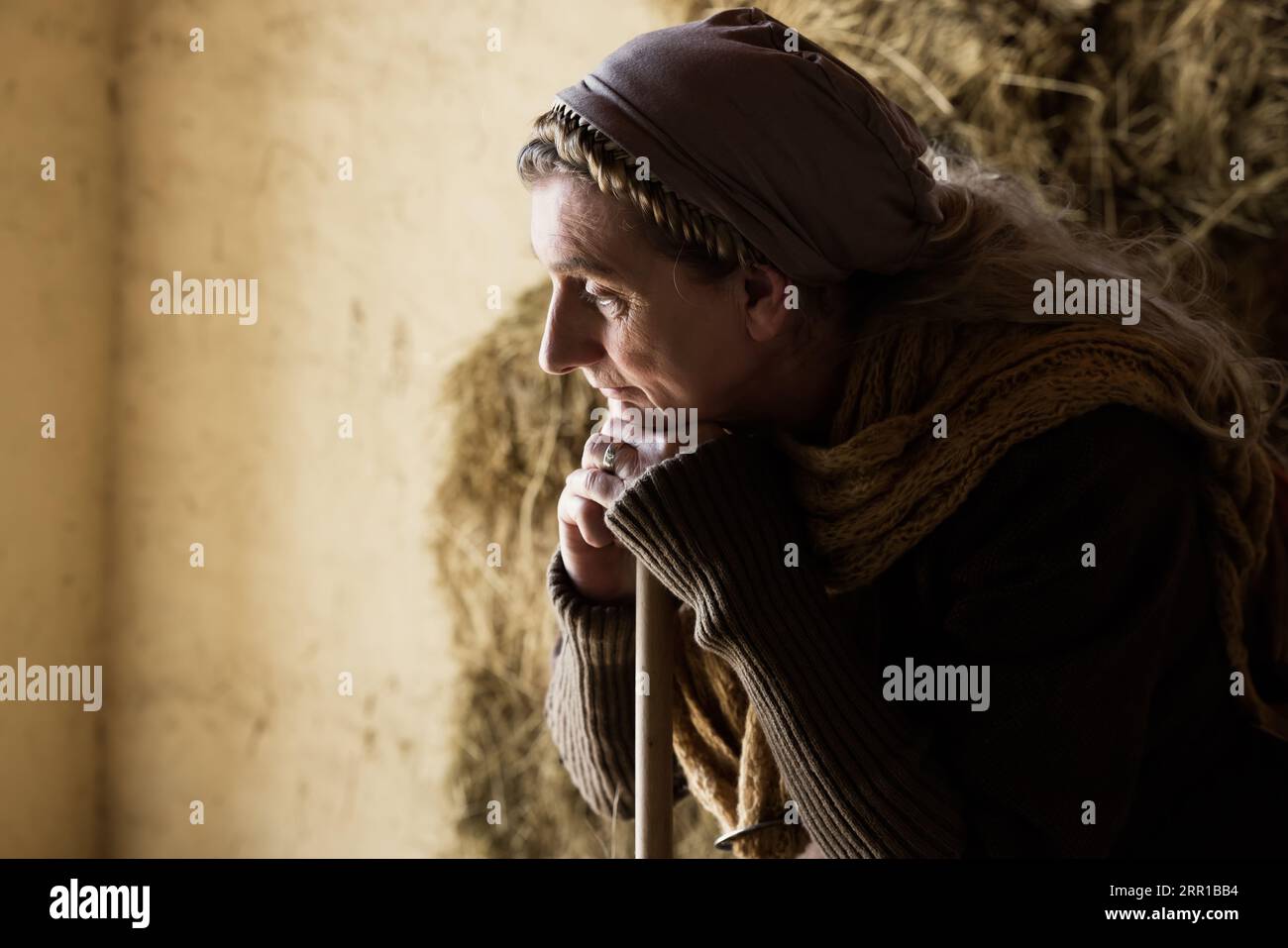 Woman in historical medieval costume working with a broom in a hay shed ...