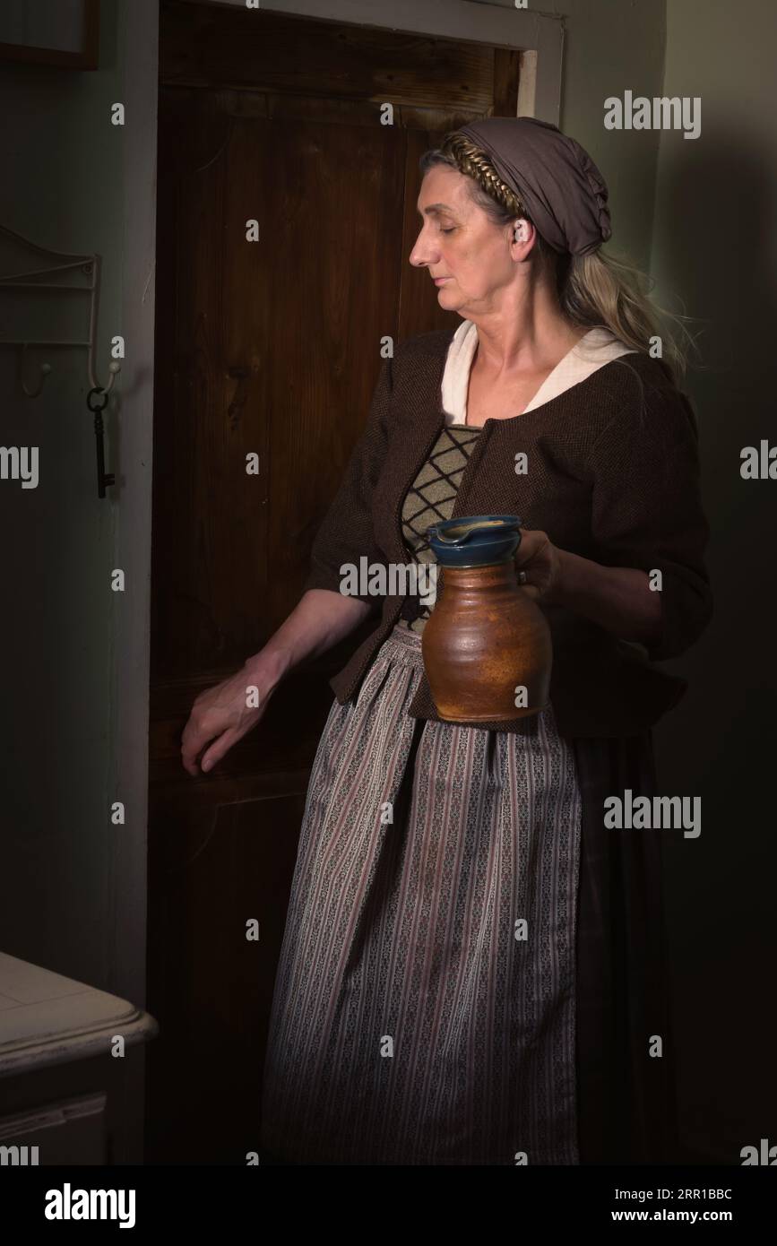 Lady in medieval peasant costume entering a door with an old jug in her ...