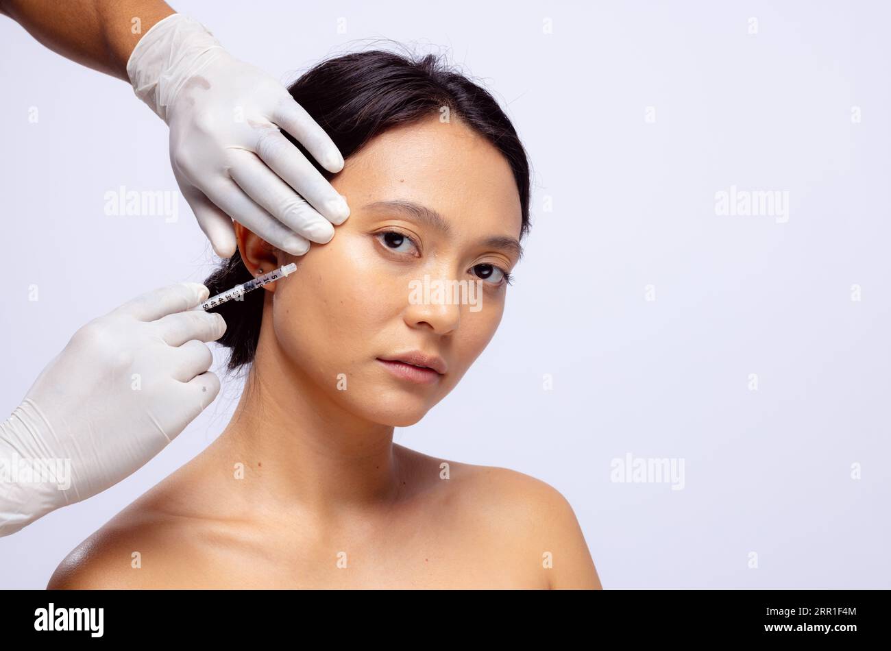 Hands of beautician in white surgical gloves injecting botox in cheek ...