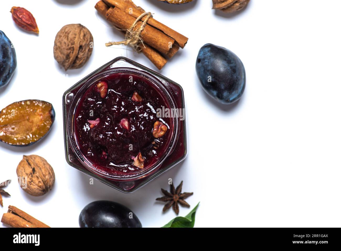 Homemade plum jam with cinnamon and walnuts, in a glass jar on a white ...