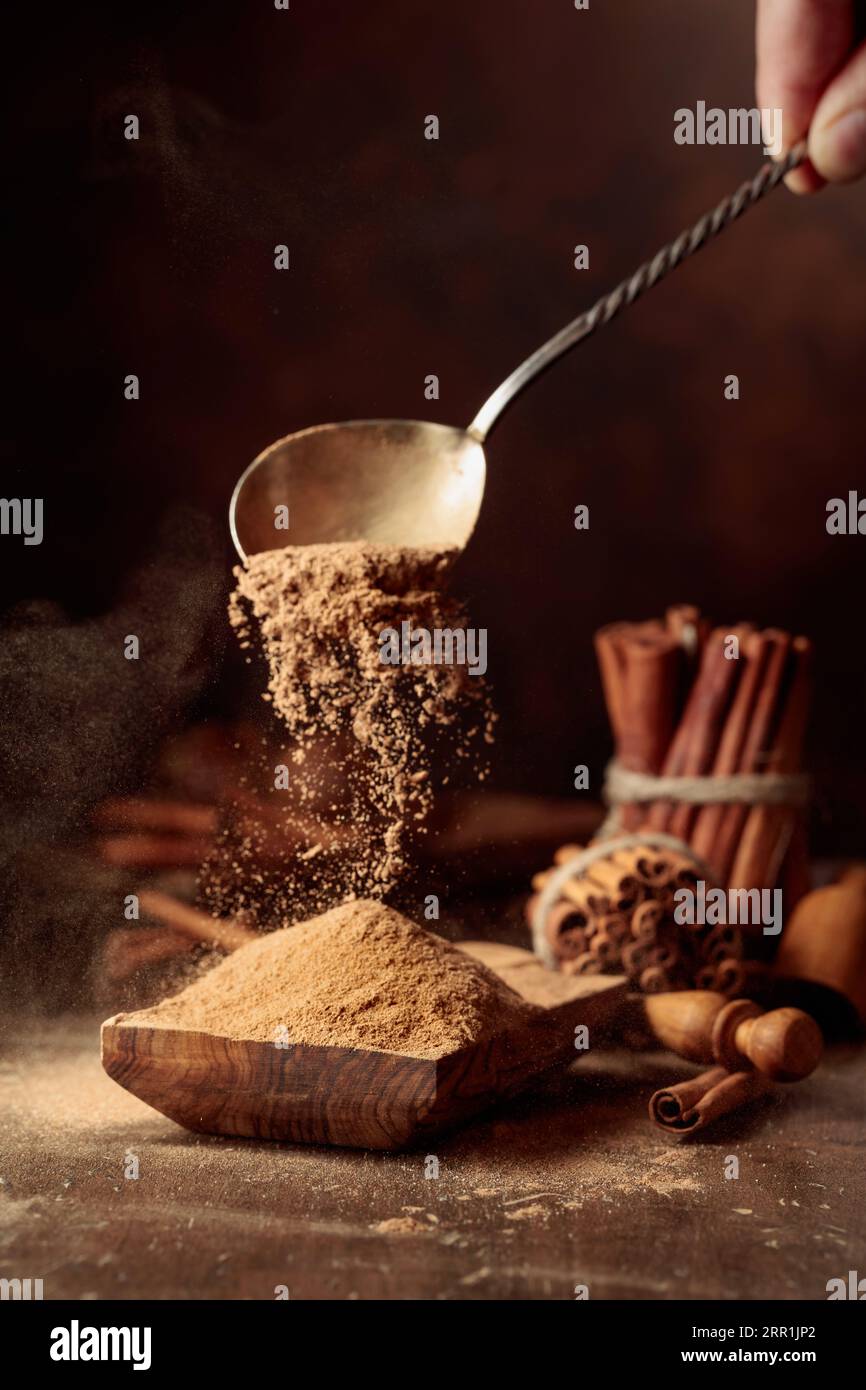 Cinnamon powder is poured into a wooden bowl. In the background are ...