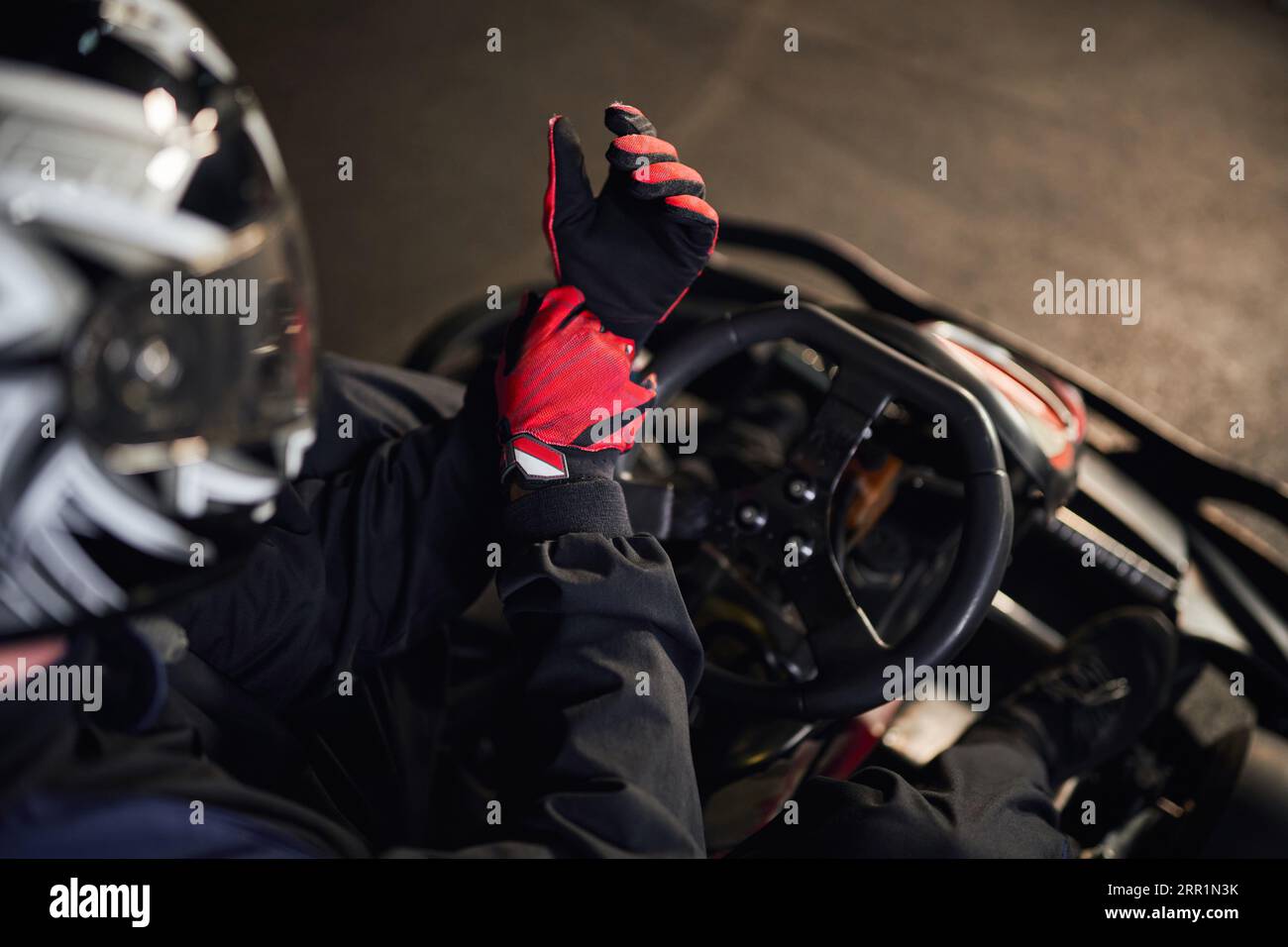 top view of go kart racer in helmet wearing red sport gloves, preparing ...