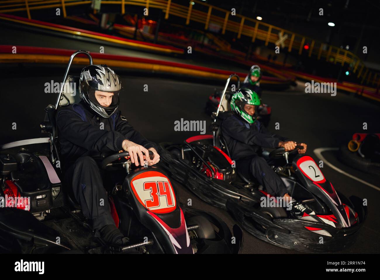focused multicultural racers driving go kart cart on indoor circuit ...