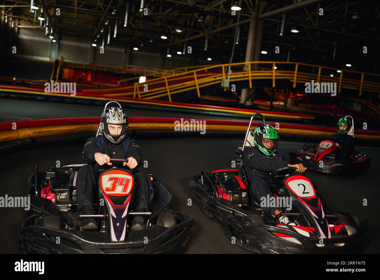 focused multicultural go cart racers driving on indoor circuit, speed ...
