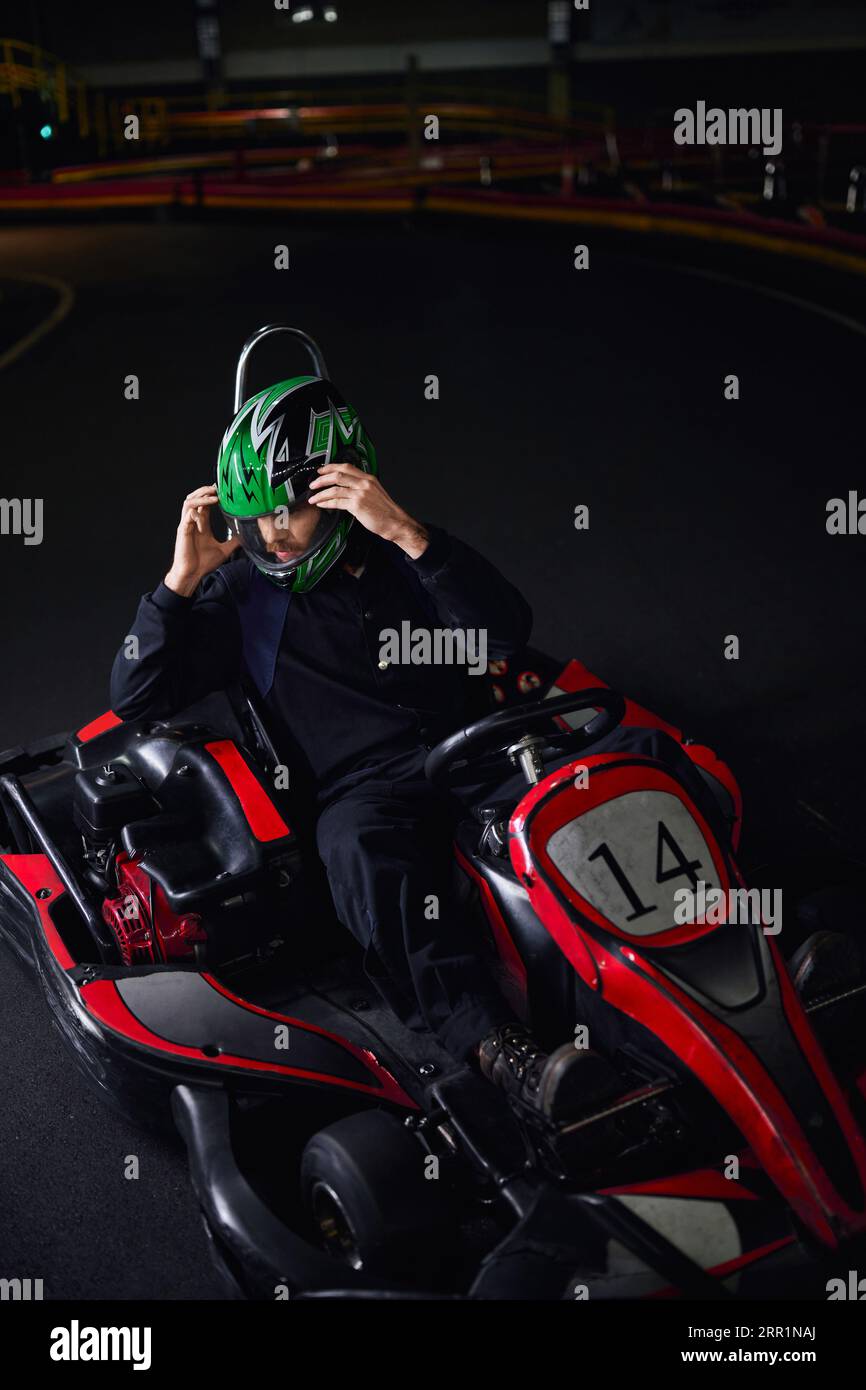 man taking off helmet and sitting in go kart after race on indoor ...