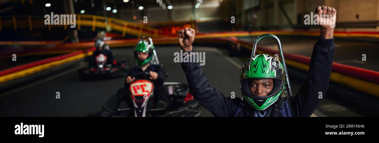 excited african american go cart driver in helmet raising hands and ...