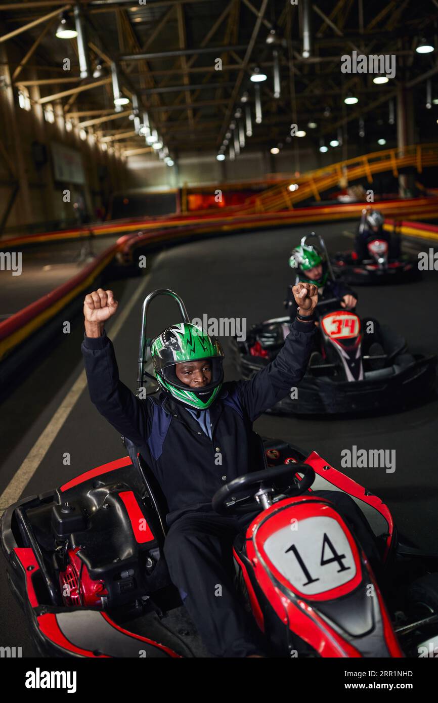 excited african american go cart driver in helmet raising hands and ...