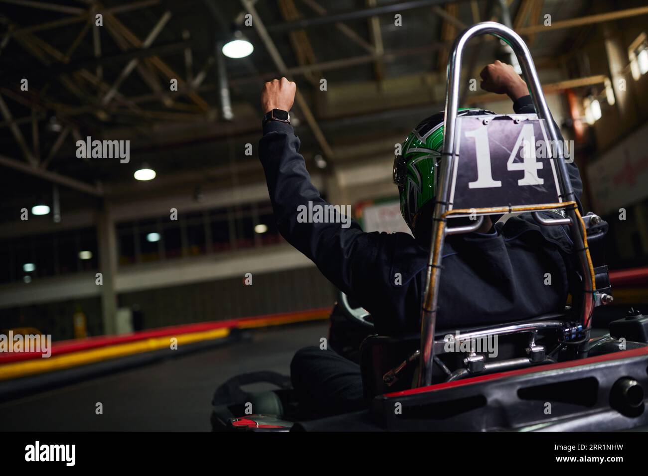 back view of motorsports driver in helmet raising hand and winning race ...