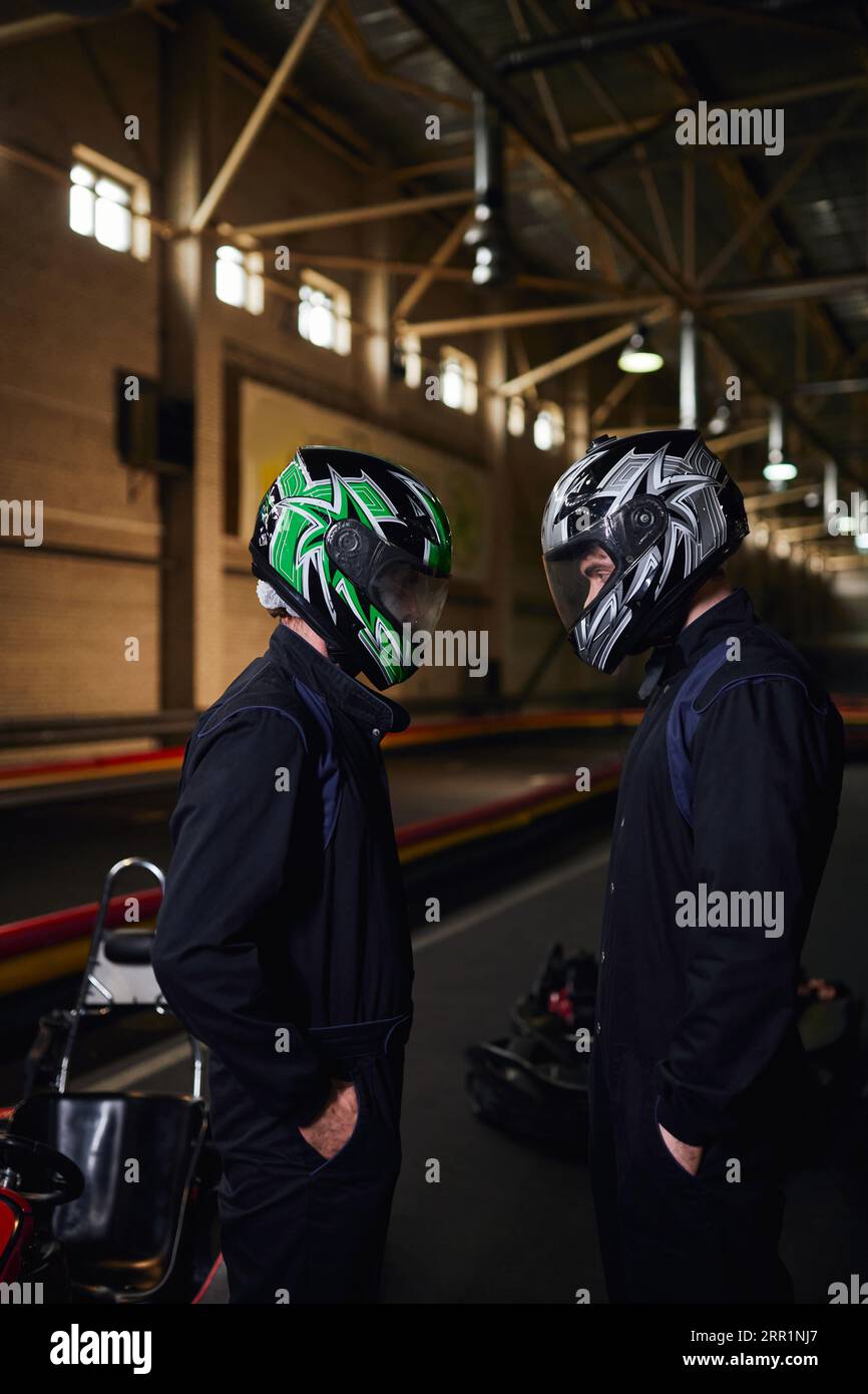 two go kart competitors in sportswear and helmets standing face to face ...