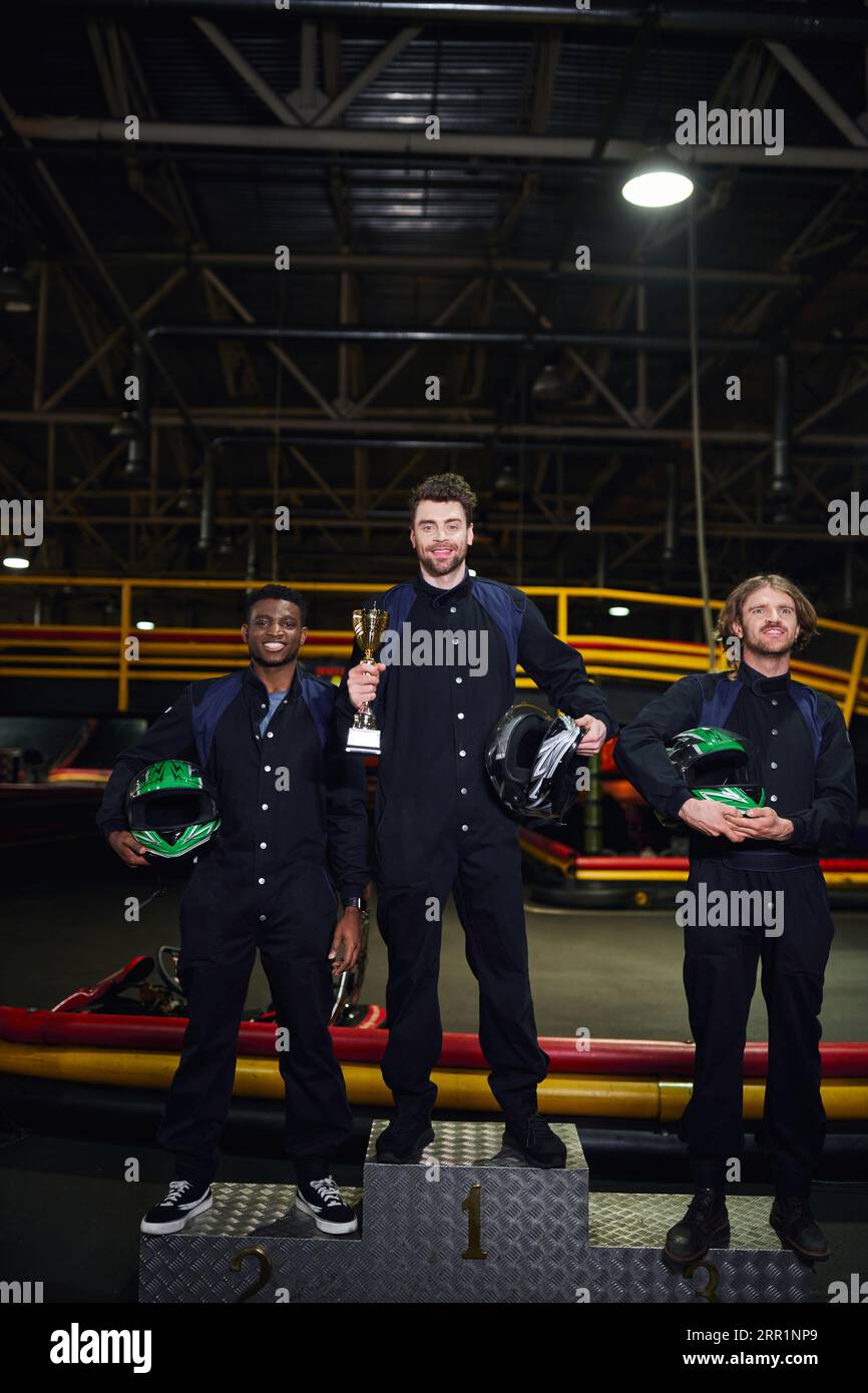 happy man holding golden cup and standing as a winner of go-kart race ...