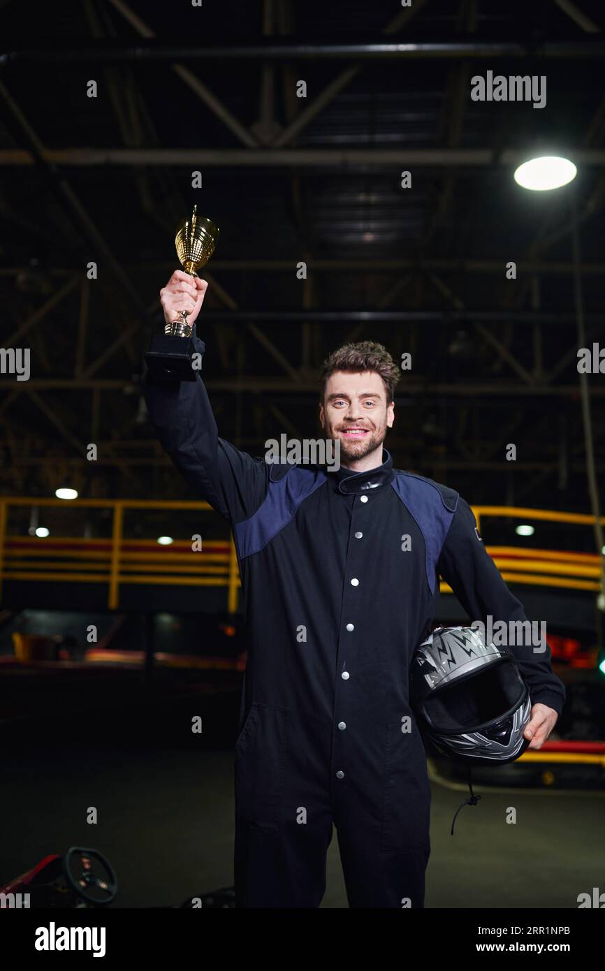 cheerful driver in sportswear holding golden cup and standing as a ...