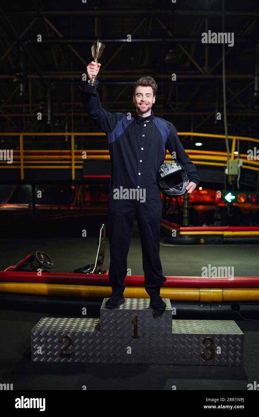 happy driver in sportswear holding golden cup and standing as a winner ...