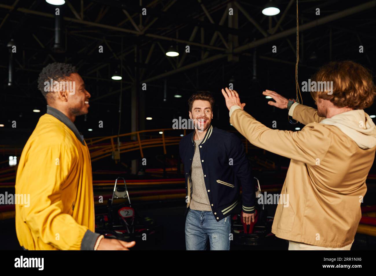 man giving high five to diverse friends inside of indoor track, go-cart concept, motorsport ...