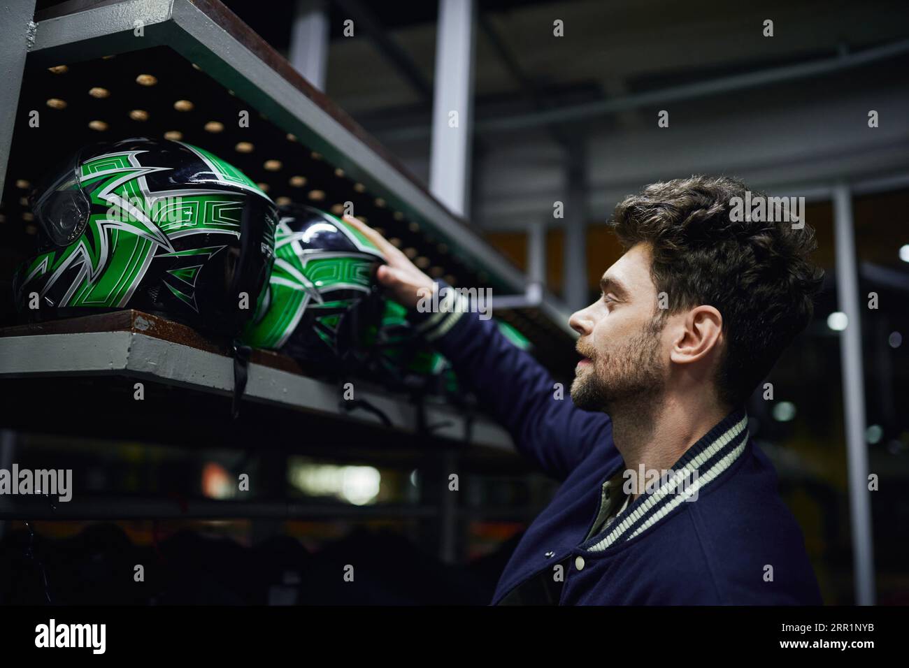 side view of handsome man choosing helmet for karting inside of karting ...