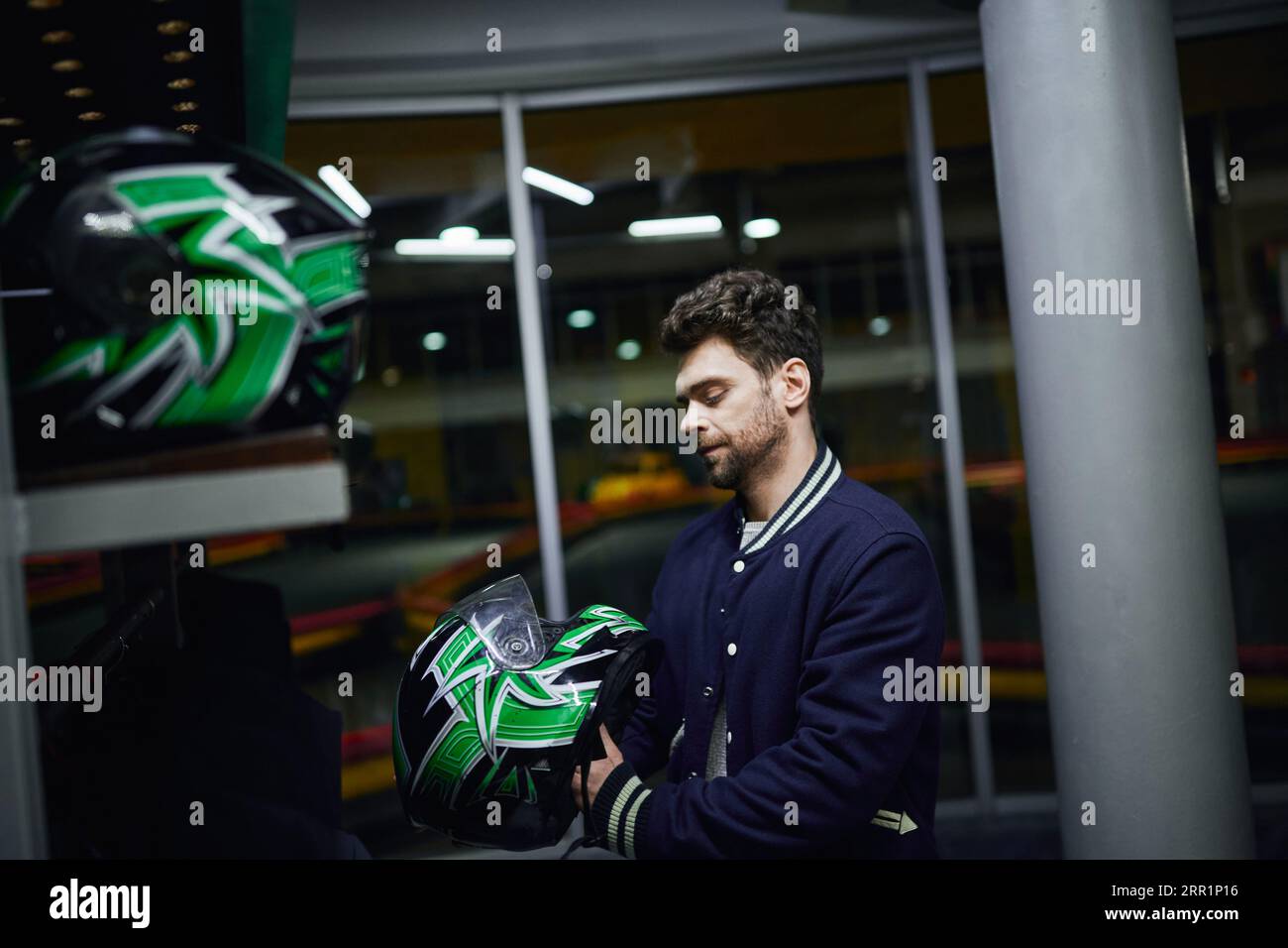 handsome man choosing helmet for karting inside of karting locker room ...