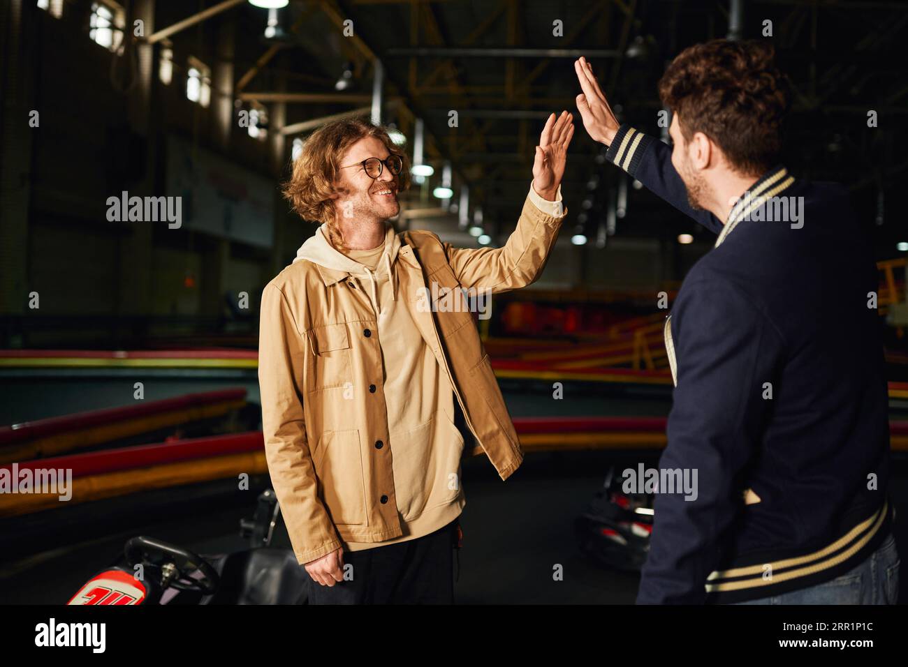 happy man in glasses giving high five to friend inside of karting ...