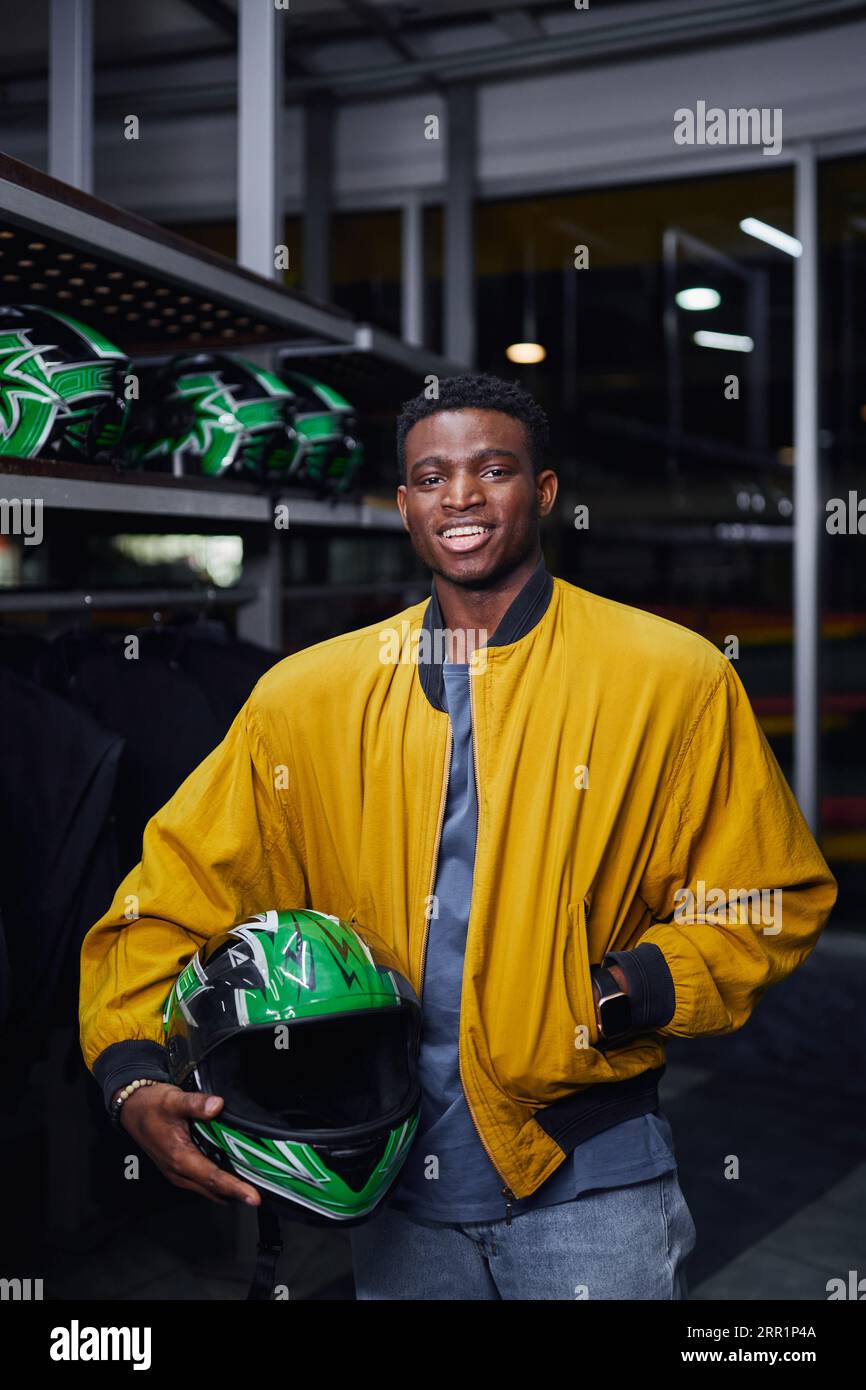 cheerful african american kart racer in yellow bomber jacket holding ...