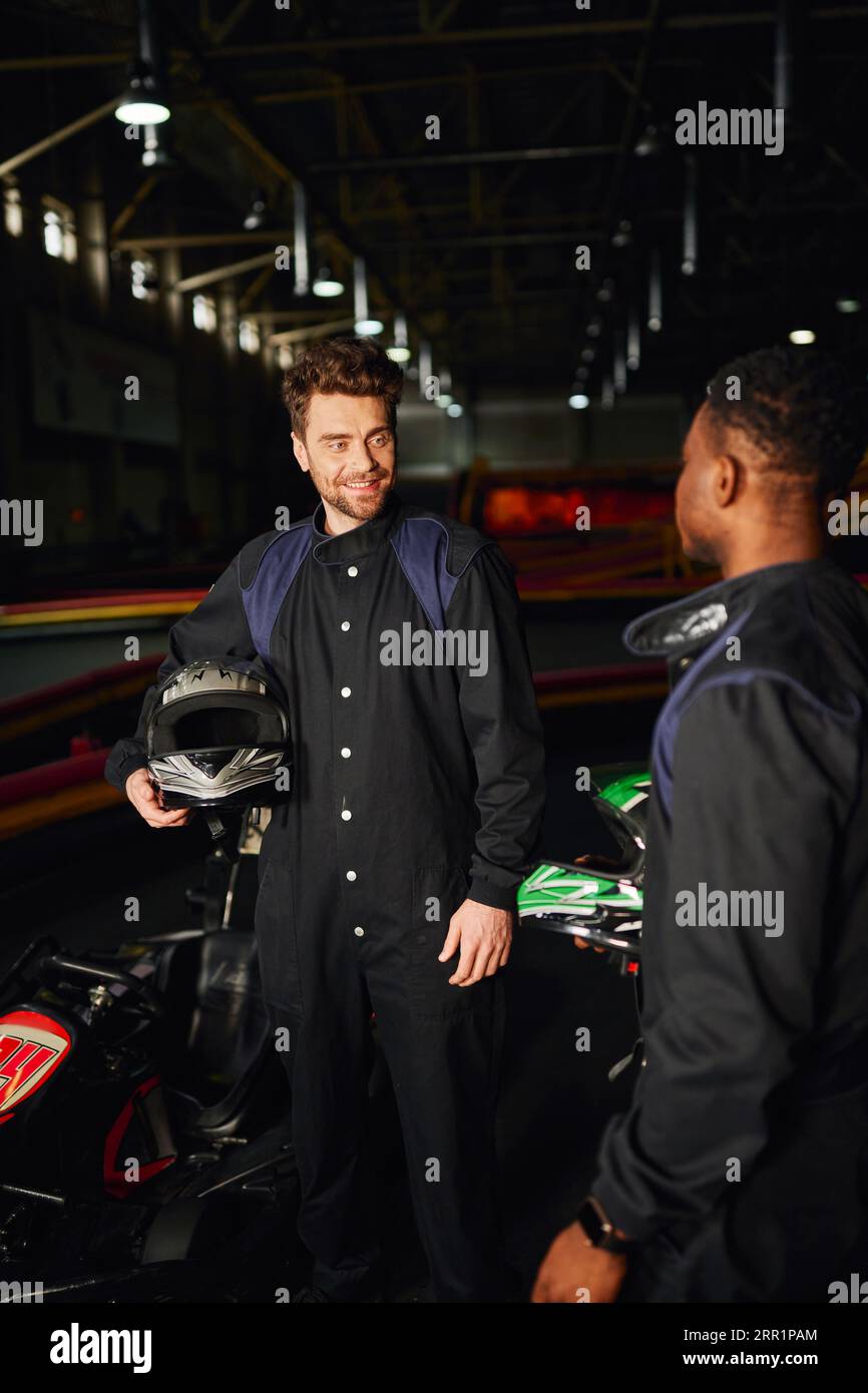 cheerful kart driver holding helmet and looking at african american ...