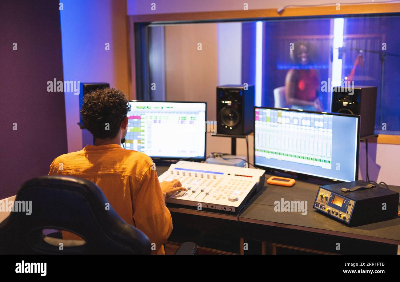 Back view of male audio engineer using mixing board and computer sound ...