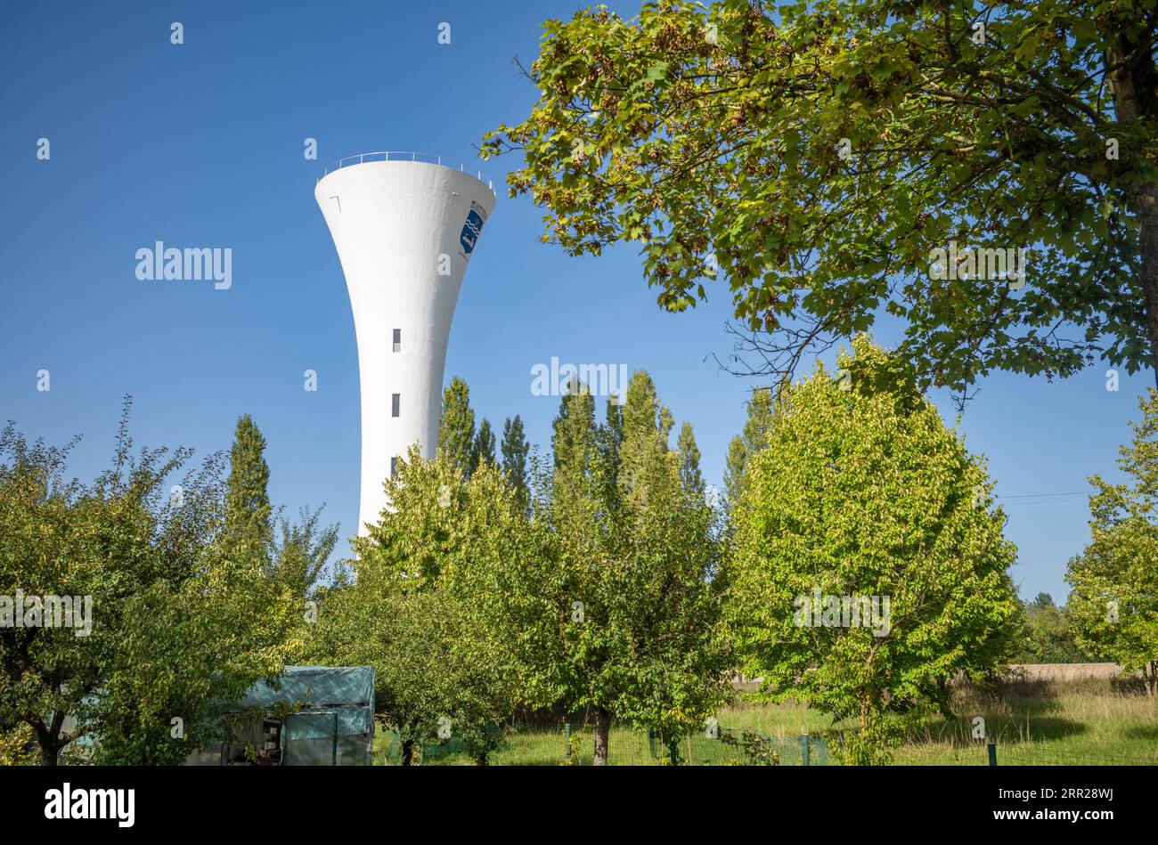 A tall, white, conical-shaped concrete water tower surrounded by trees ...