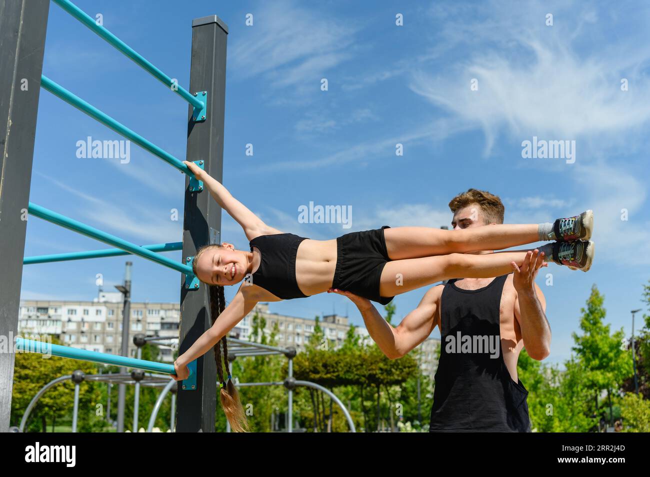 Girl doing human flag exercise with her trainer on a climbing frame ...