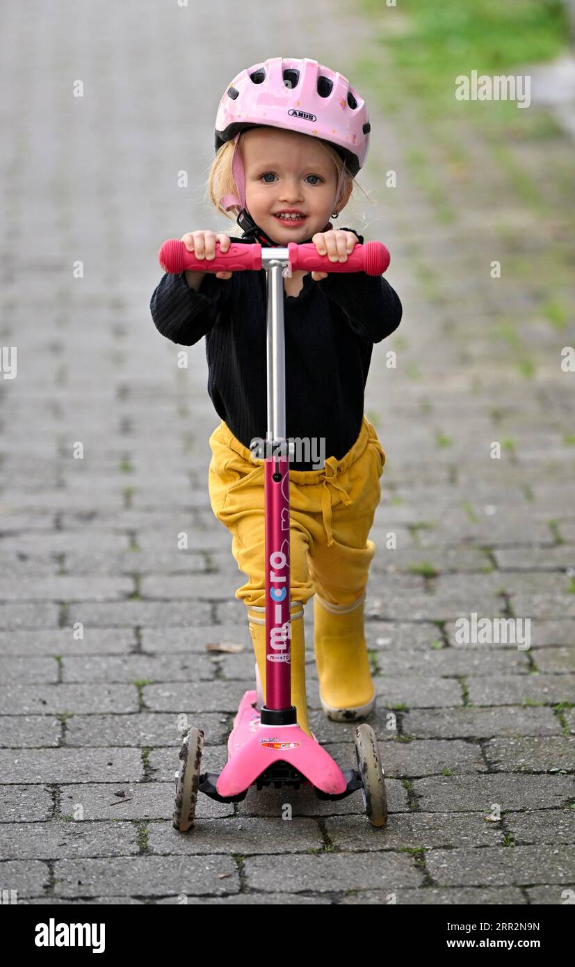 Little girl, blond, 2 years, rides scooter, crash helmet, urban ...
